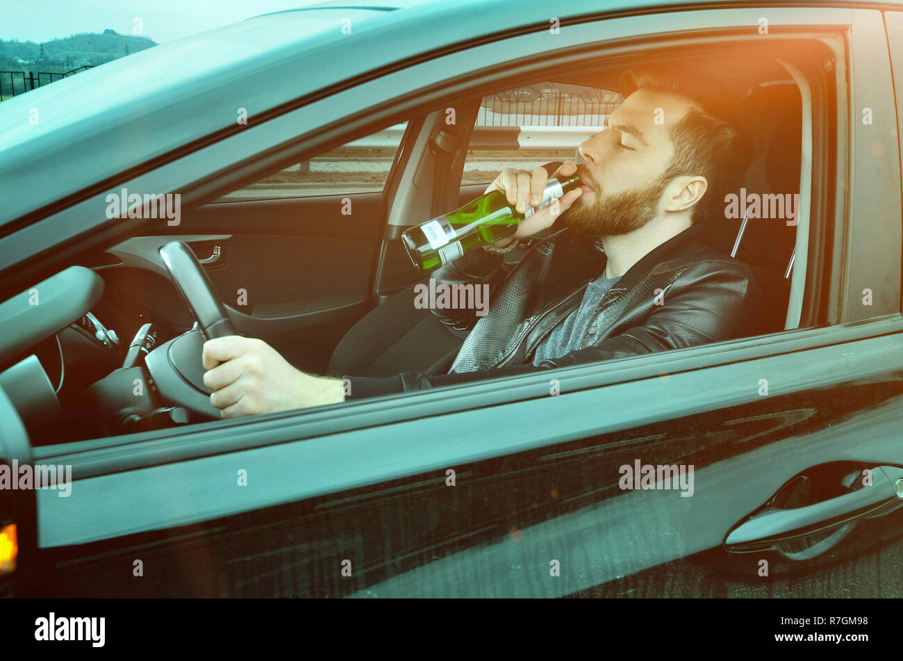 A drunken man driving a car with a bottle of alcohol in his hand. A Man ...