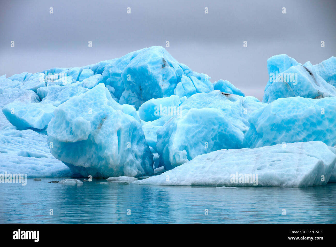 big blocks of blue ice of a glacier floating on the water with a gray ...