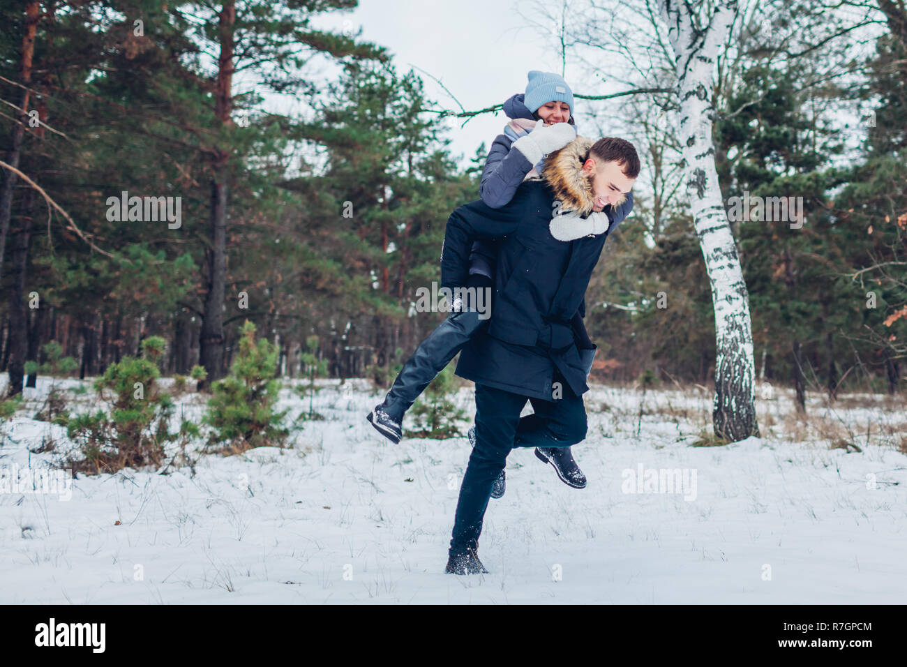 Guy giving his girlfriend piggyback in winter forest. Youn loving ...