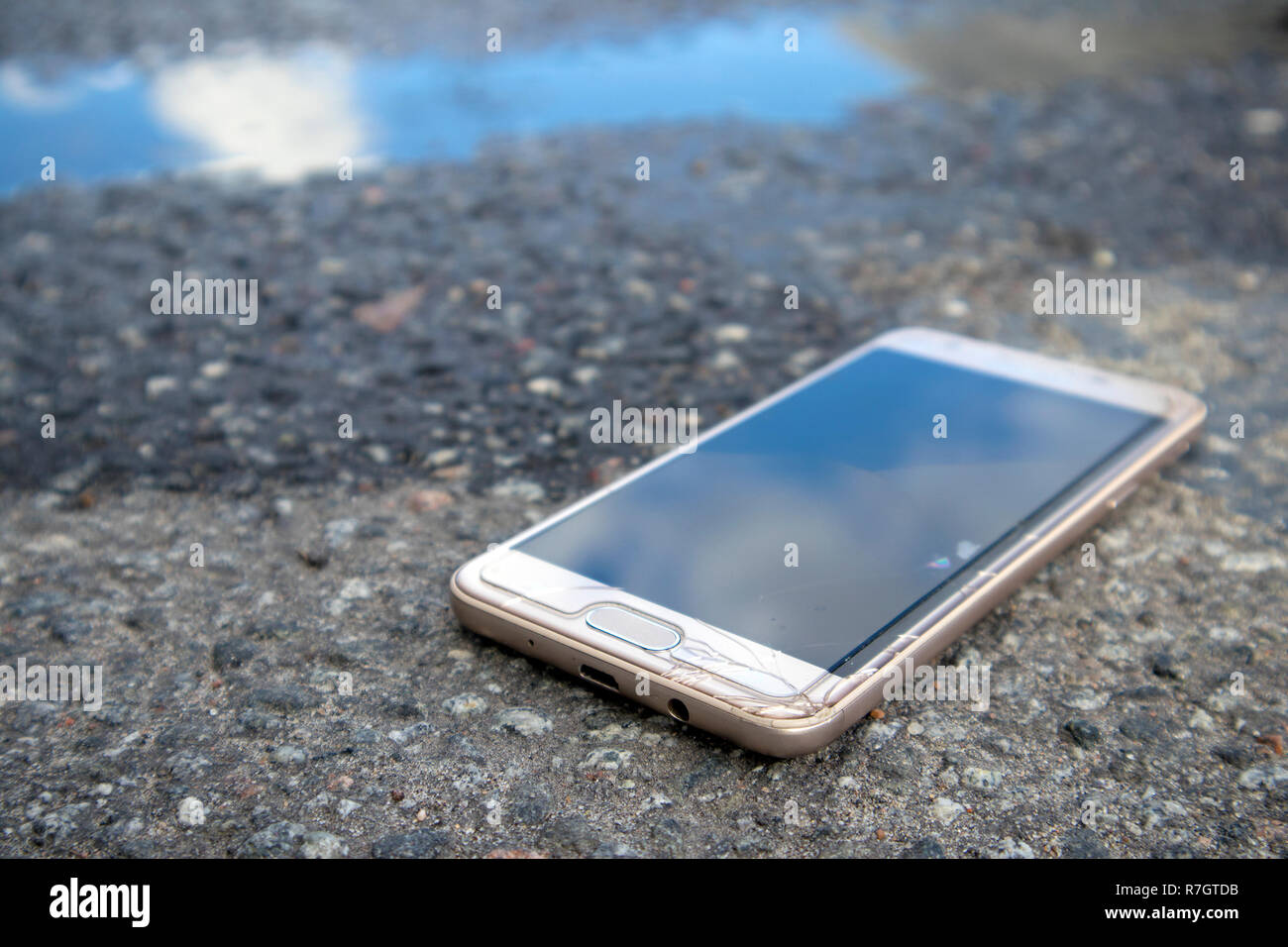 Modern smart phone with cracked screen glass lying in a puddle on the ...
