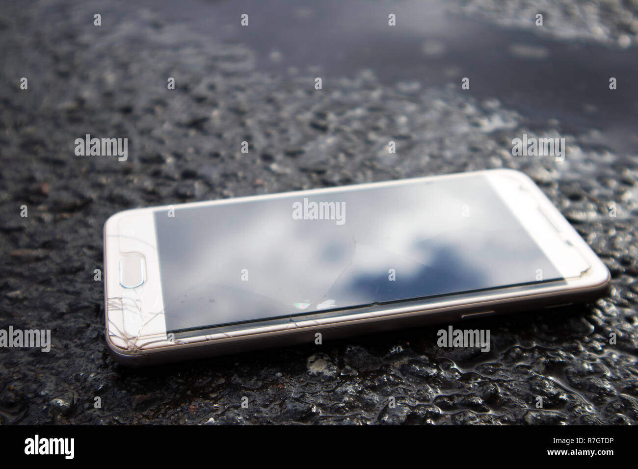 Modern smart phone with cracked screen glass lying in a puddle on the ...