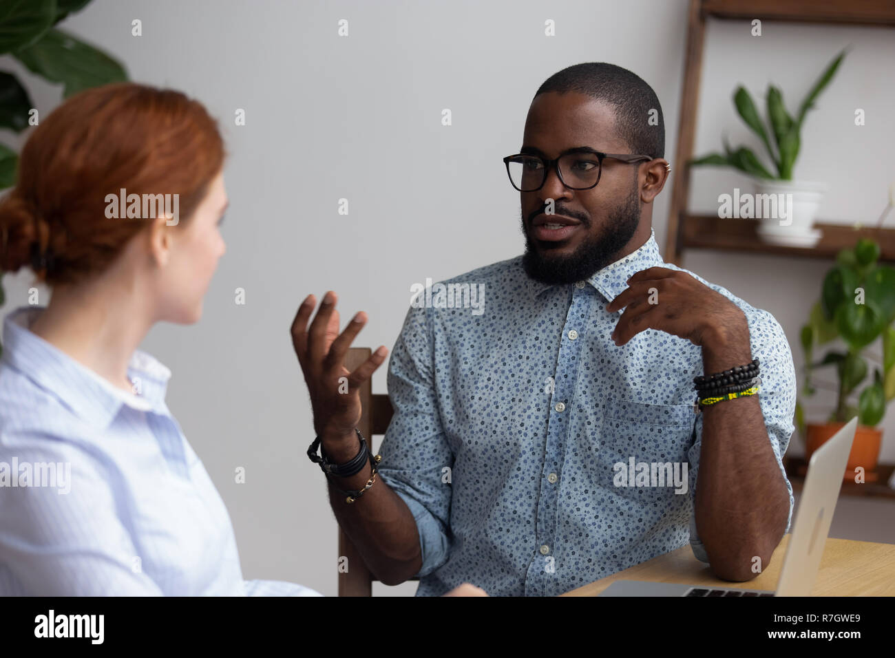 Black and caucasian teammates talking sitting in office desk Stock ...