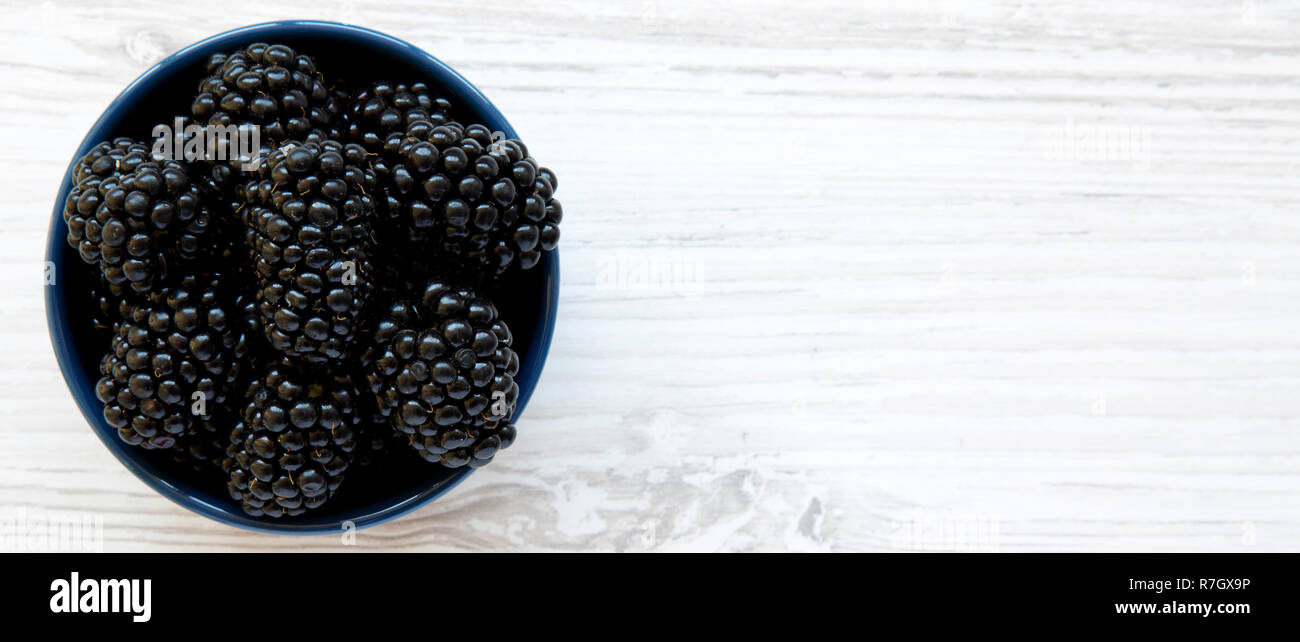 Full blue bowl of blackberries over white wooden surface, overhead view ...