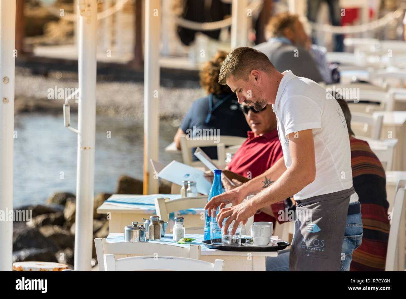 Mykonos, Greece - October 12th, 2018: A male waiter clearing a table ...