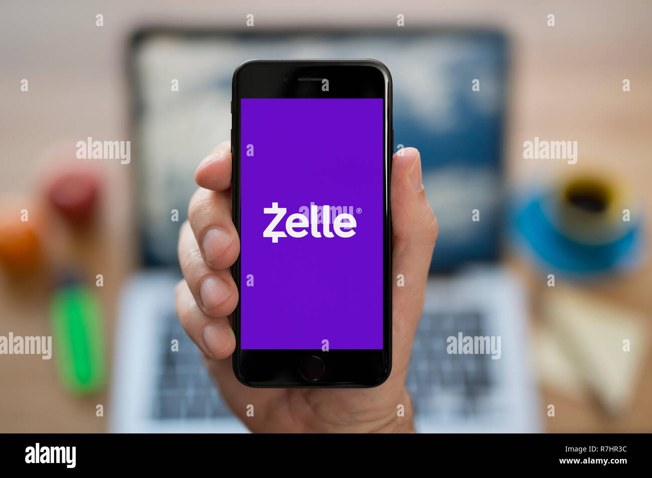 A man looks at his iPhone which displays the Zelle logo (Editorial use ...