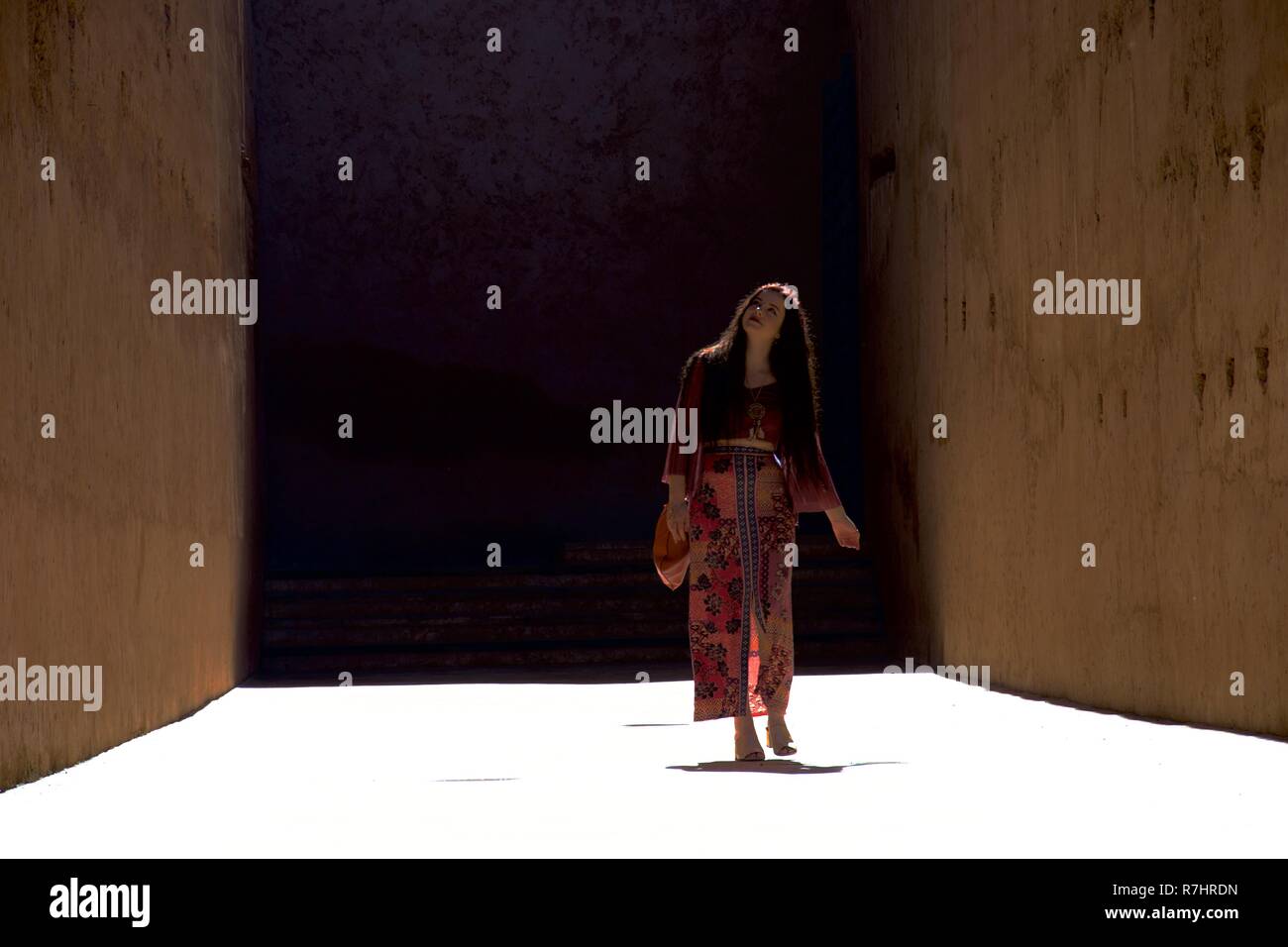 A lady in red and pink walks towards us down a vividly lit road ...