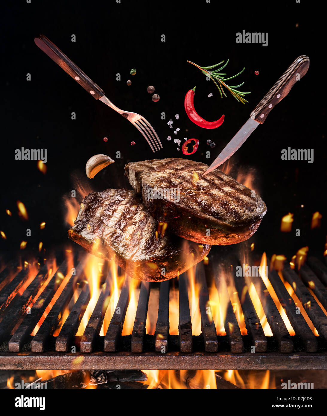 Raw beef steaks with vegetables and spices fly over the blazing grill ...