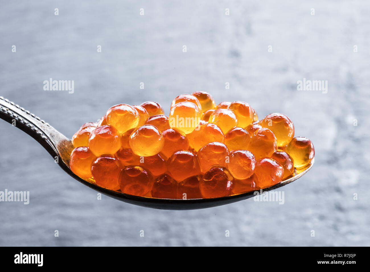 Silver spoon of red caviar on gray graphite background. Macro picture ...