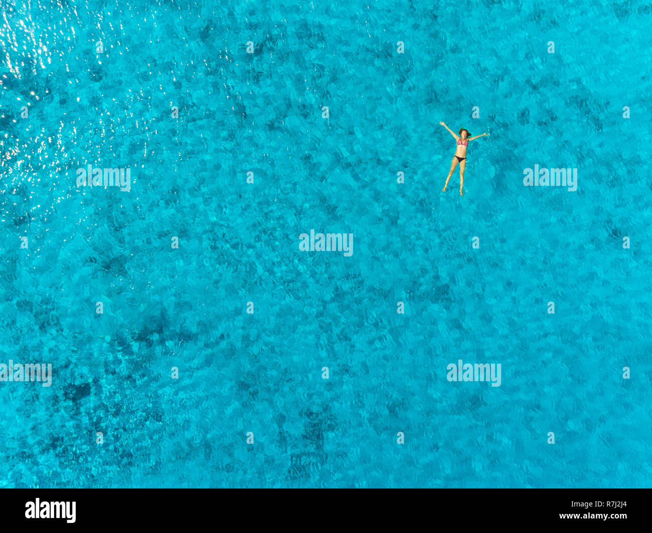 High aerial view of pregnant woman floating on her back in transparent ...