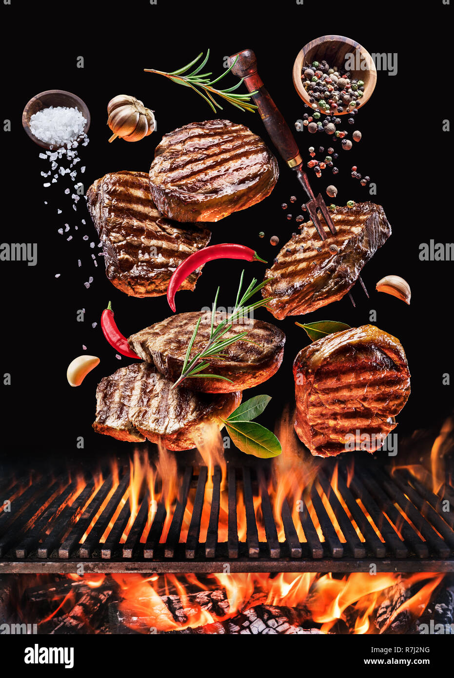 Grilled beef steaks with vegetables and spices fly over the blazing ...