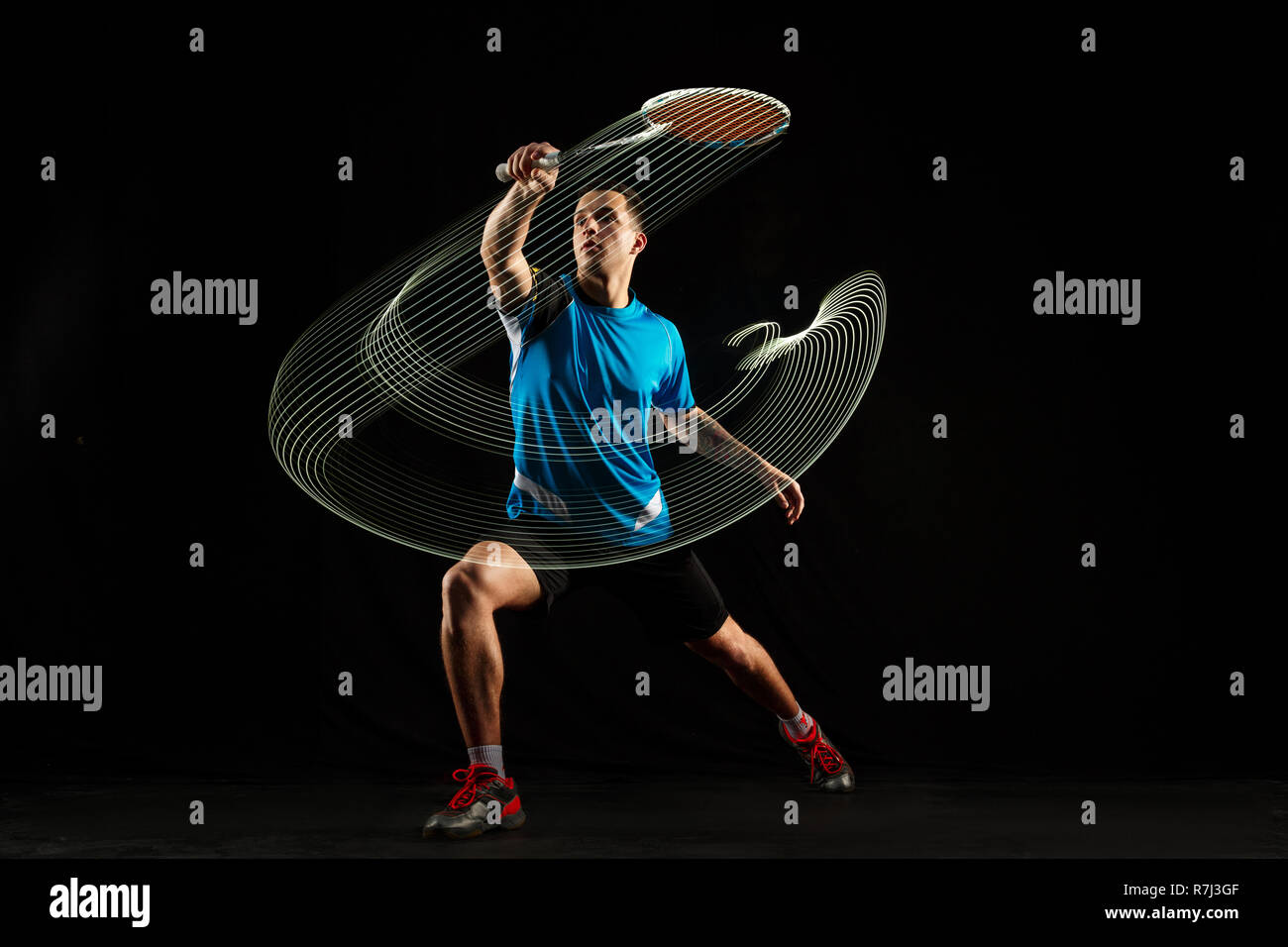 Young man playing badminton over black studio background. Fit male ...