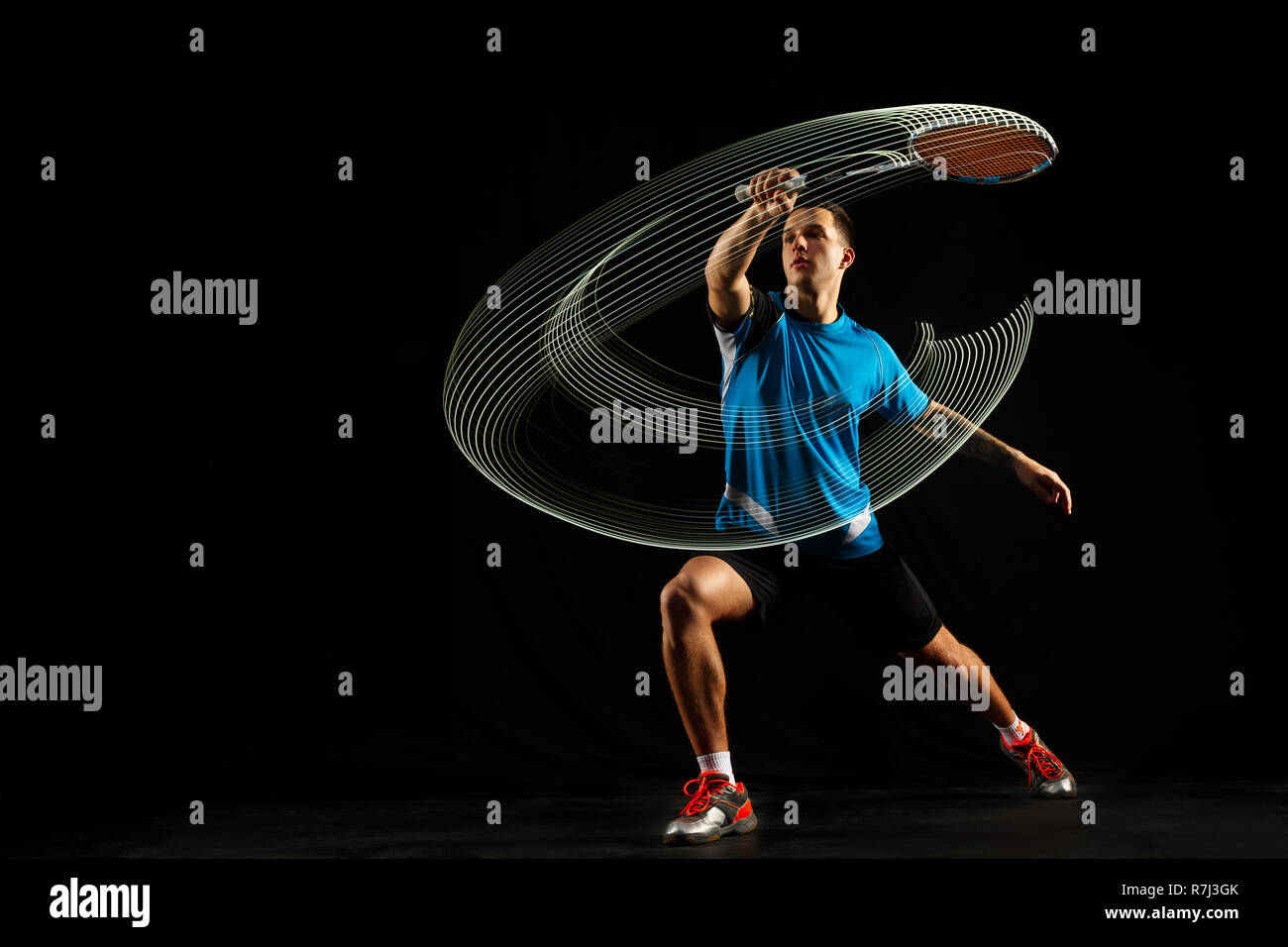 Young man playing badminton over black studio background. Fit male ...