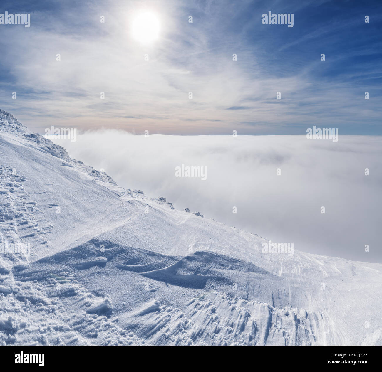 Mountain tops covered with snow above the white heavy clouds. The Sun ...