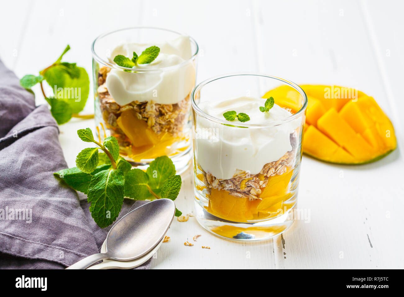 Greek yogurt mango granola parfait in a glass on a white wooden ...