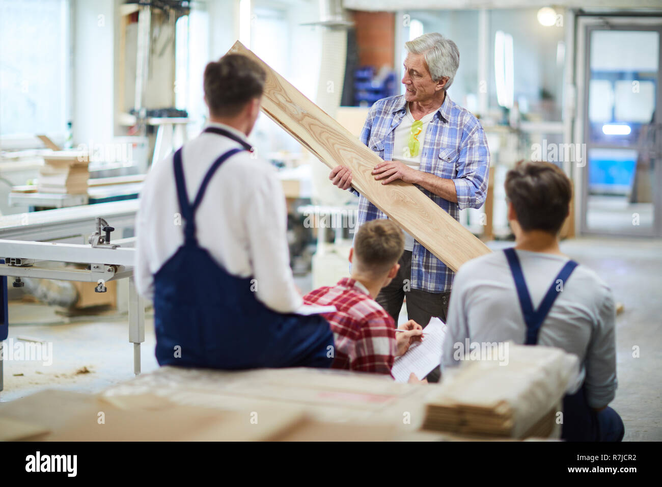 Confident carpenter teaching students to process wood Stock Photo - Alamy