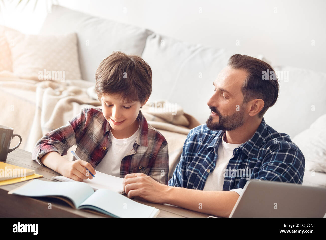 Father and son at home sitting at table doing homework together joyful ...