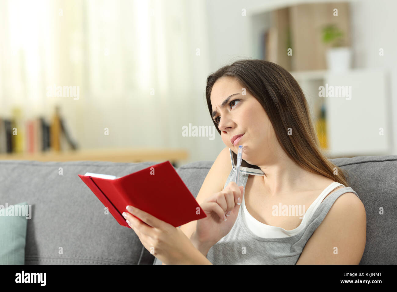 Confused woman on the phone holding an agenda sitting on a couch in the ...