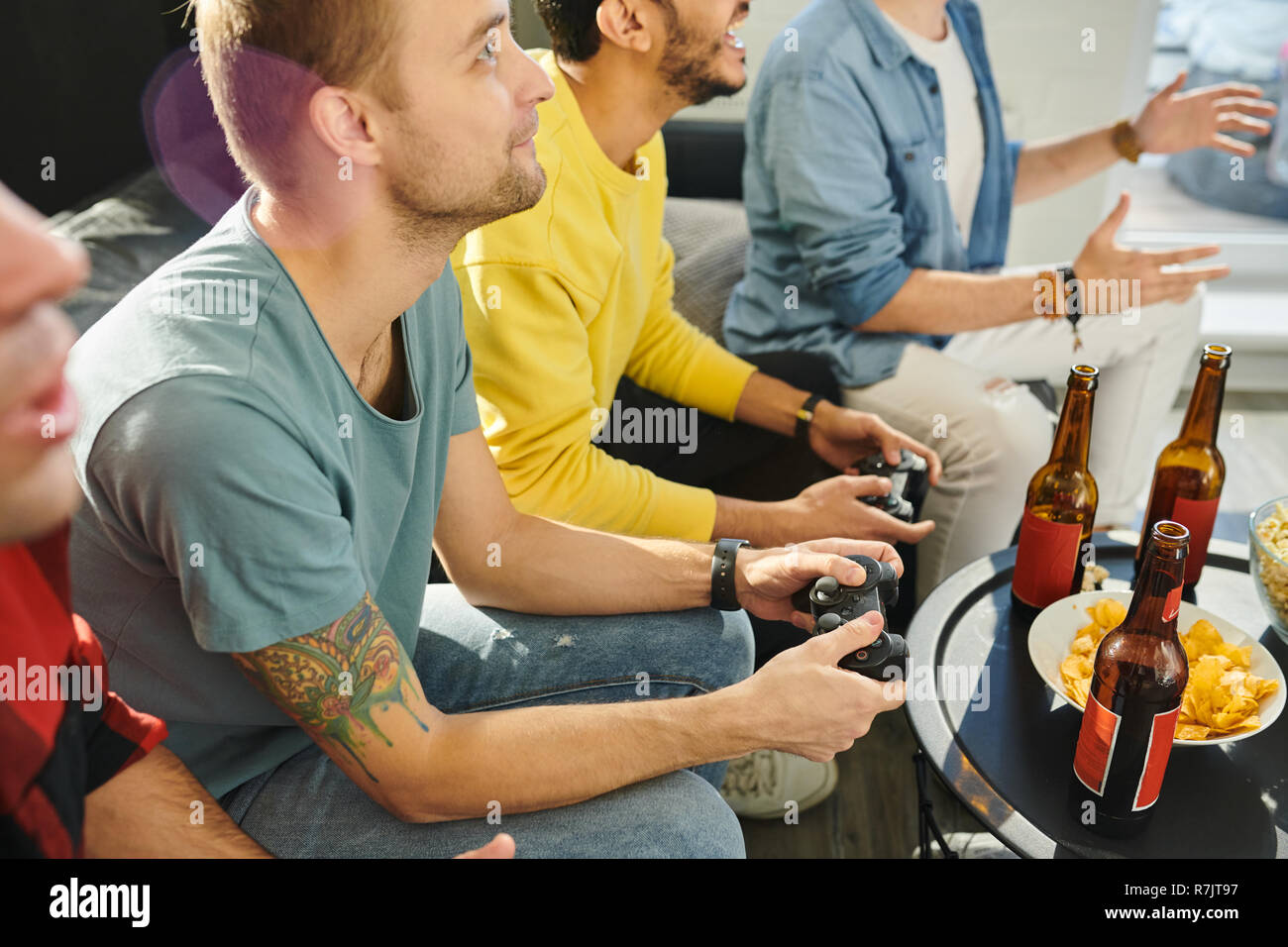 Concentrated young man sitting on sofa with joystick and playing with ...