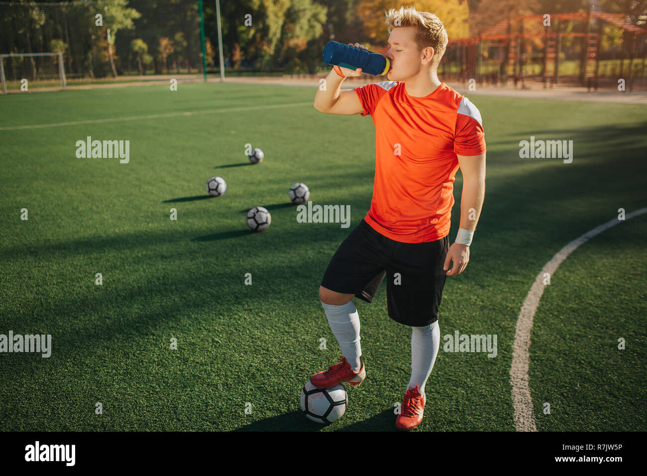 Picture of young football player stand on lawn and drink water. He hold ...