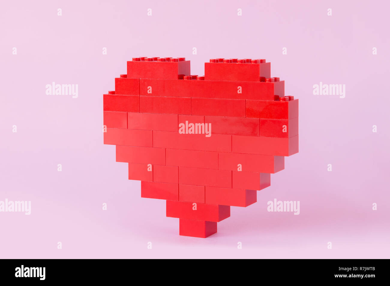 Side view of a red heart made of toy building bricks, on pink ...