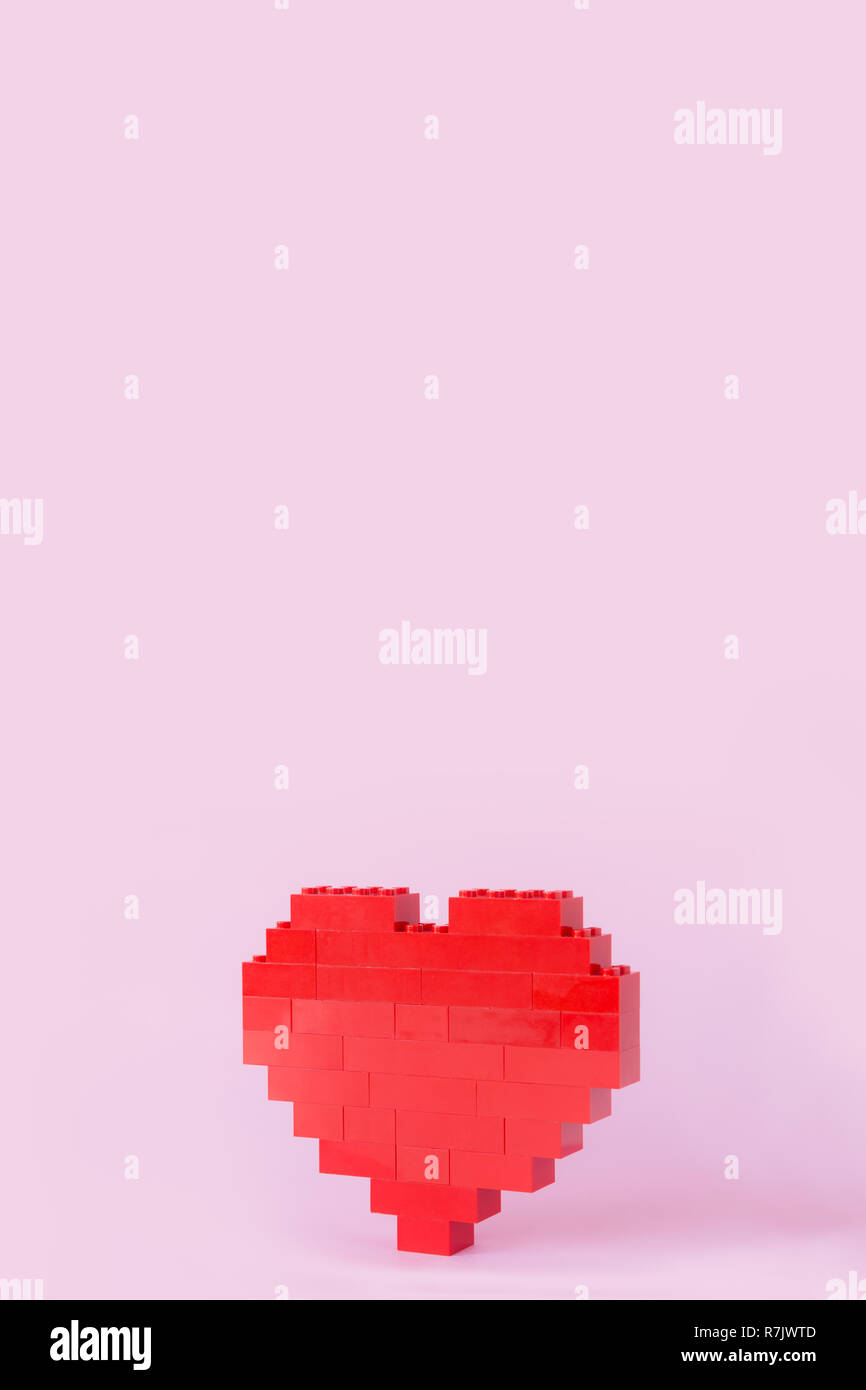 Side view of a red heart made of toy building bricks, on pink ...
