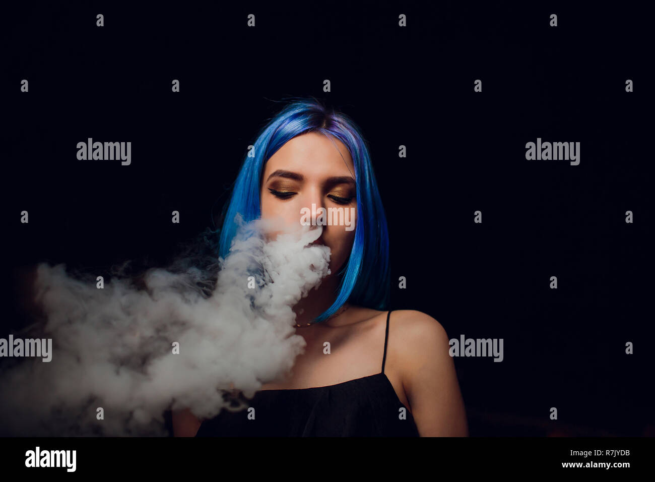 young woman smoking electronic cigarette against a black background ...