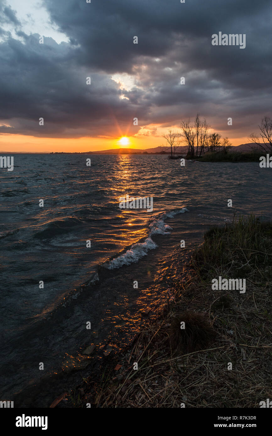 Beautiful sunset on a lake, with tree silhouettes and sun coming down ...