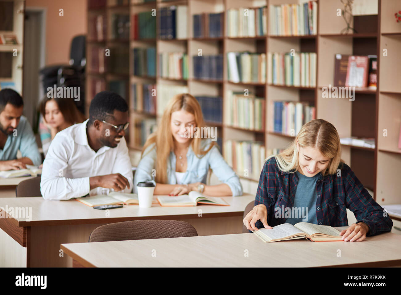 group of happy students reading books and preparing to exam in library ...