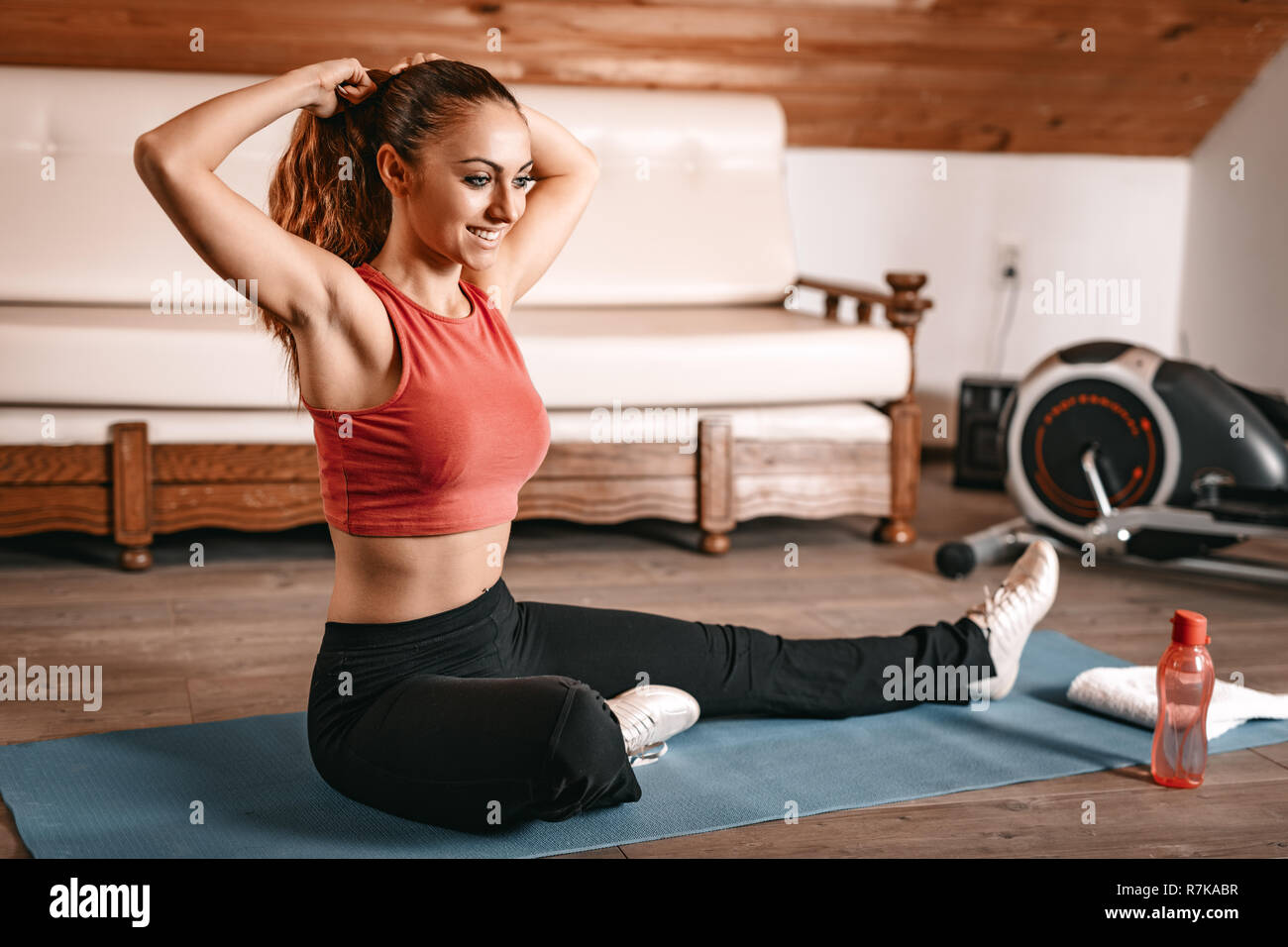 Beautiful young woman getting ready for workout at home. She is binds ...