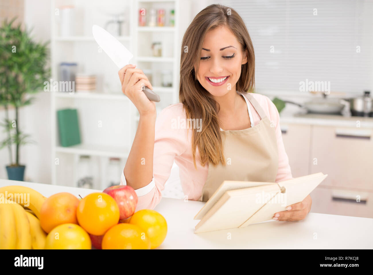 Beautiful young woman reading cookery book in the kitchen Stock Photo ...