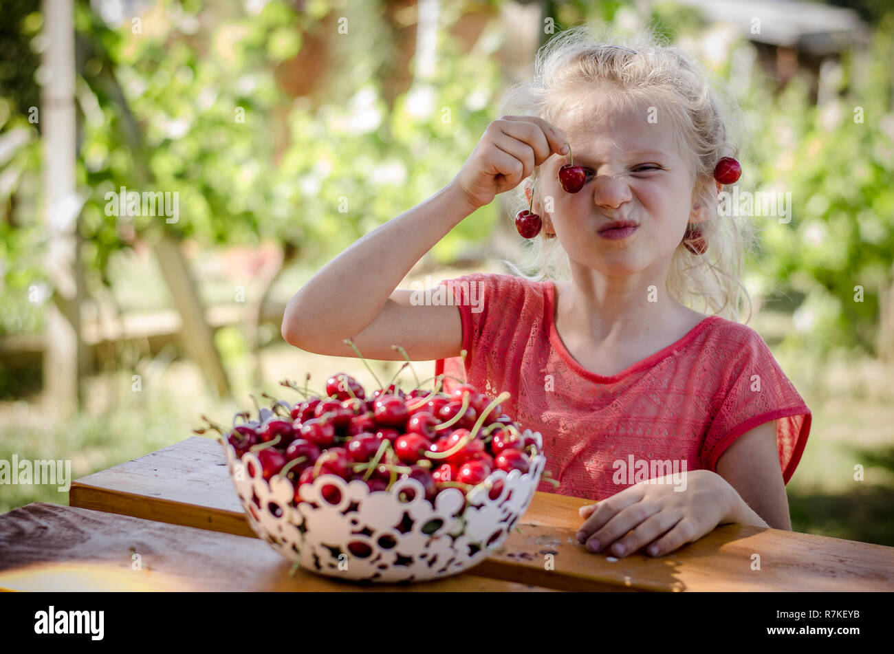 adorable blond girl eating cherry fruit in the garden Stock Photo - Alamy