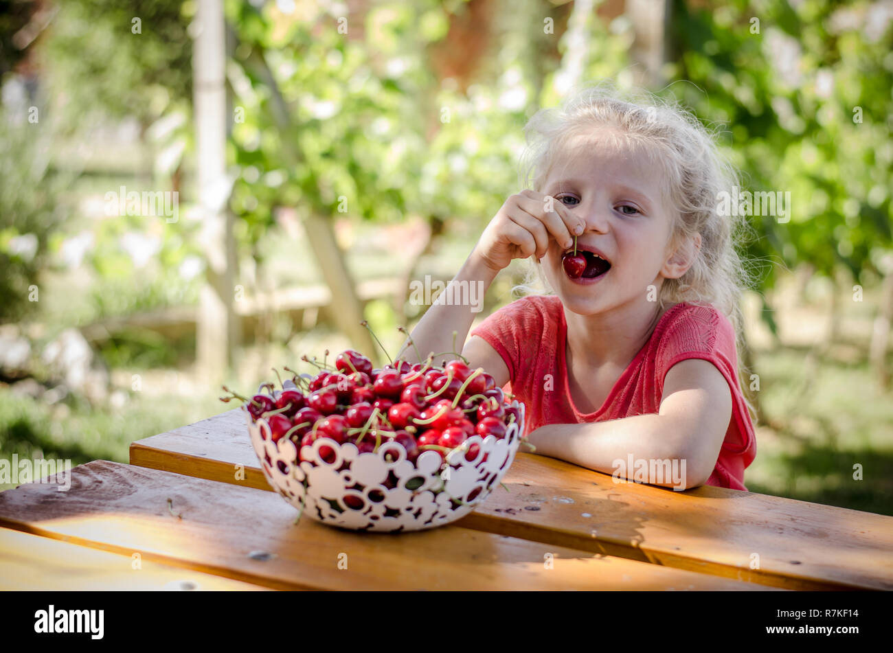 adorable blond girl eating cherry fruit in the garden Stock Photo - Alamy