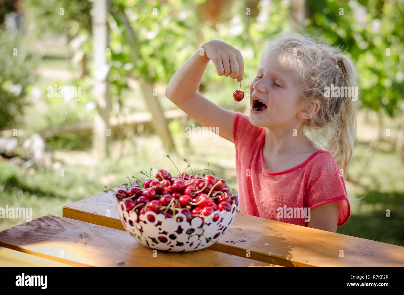 lovely blond girl eating cherry outdoors in the garden Stock Photo - Alamy