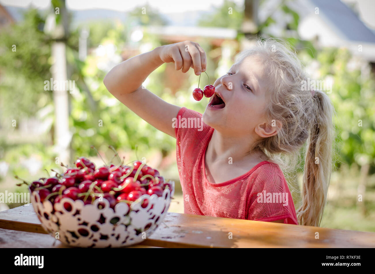lovely blond girl eating cherry outdoors in the garden Stock Photo - Alamy