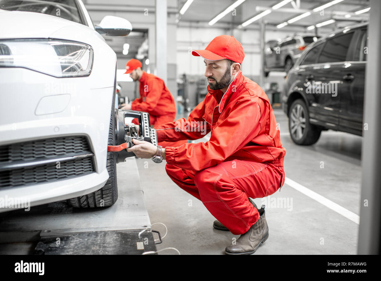 Two auto mechanics in red uniform fixing disk for wheel alignment on a ...