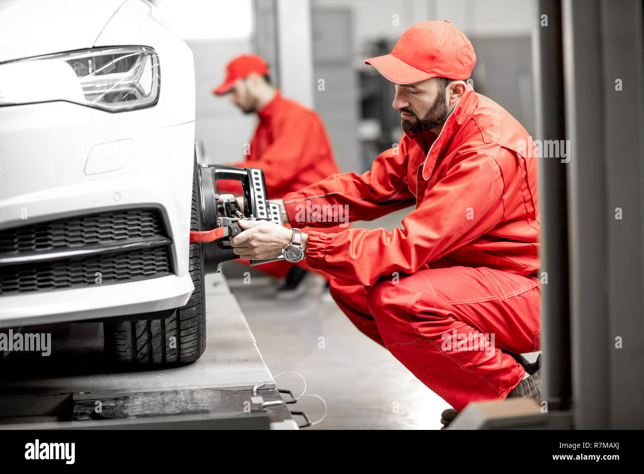 Two auto mechanics in red uniform fixing disk for wheel alignment on a ...