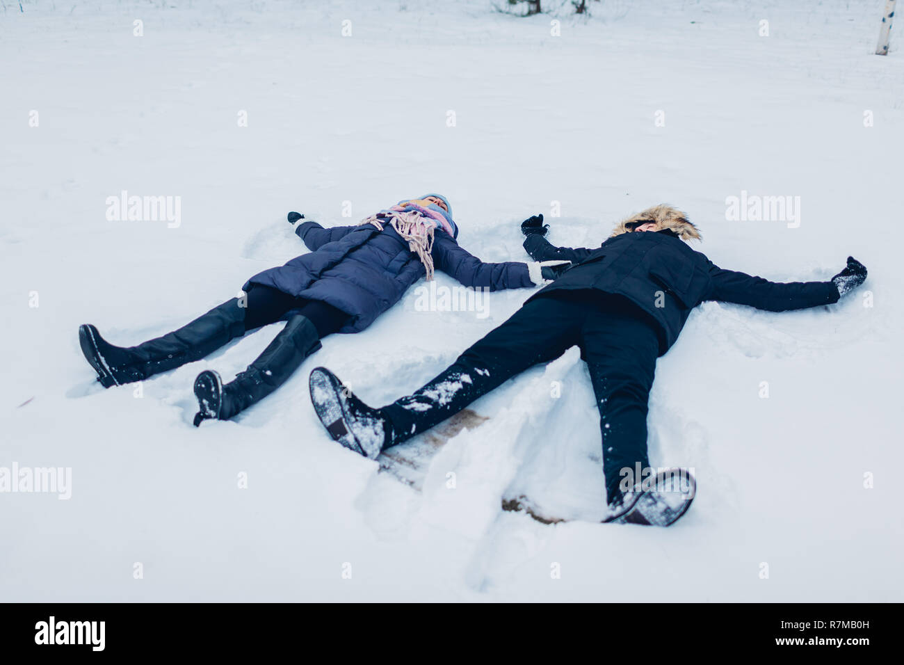 Beautiful loving couple making snow angels in winter forest lying in ...
