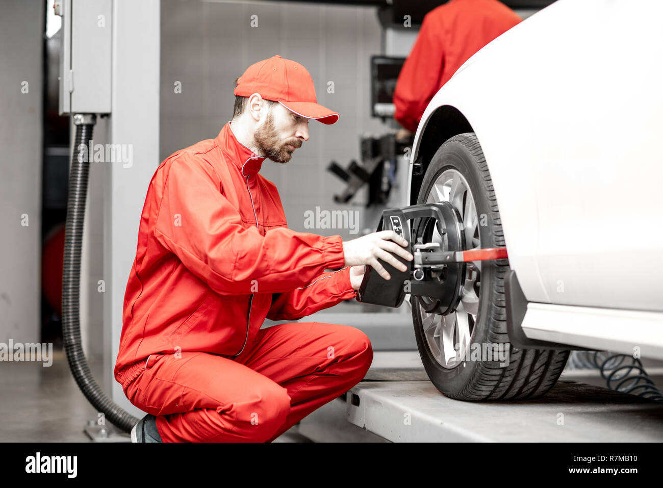 Handsome auto mechanic in red uniform fixing disk for wheel alignment ...