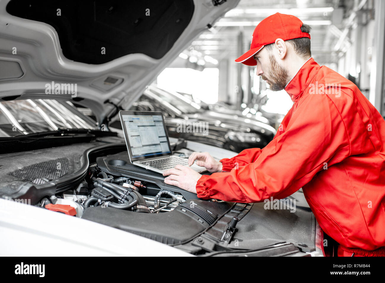 Handsome auto mechanic in red uniform doing engine diagnostics with ...