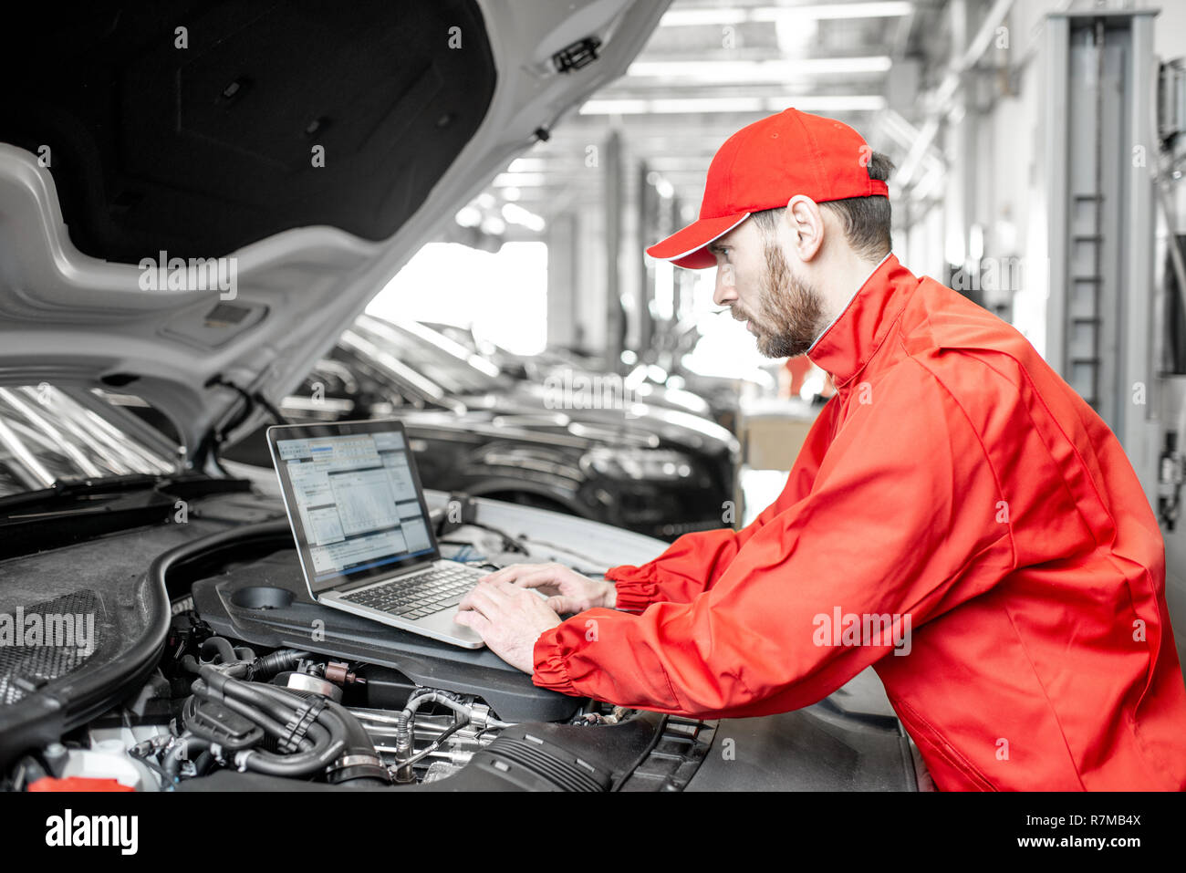 Handsome auto mechanic in red uniform doing engine diagnostics with ...