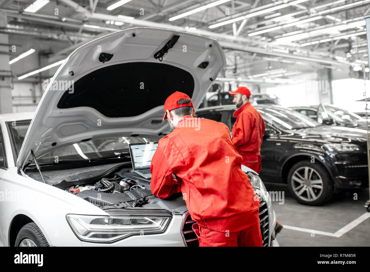 Two auto mechanics in red uniform doing engine diagnostics with ...