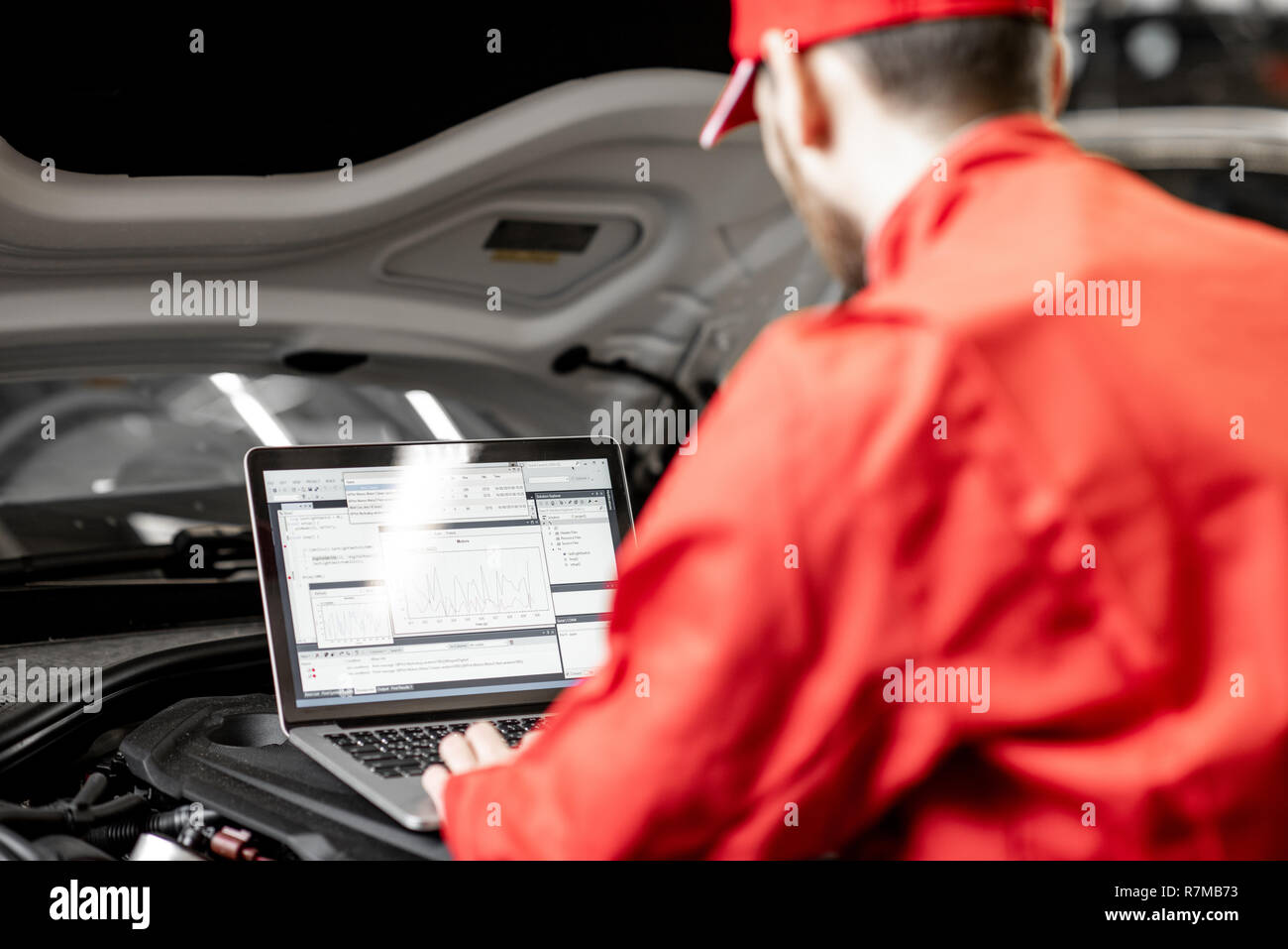 Handsome auto mechanic in red uniform doing engine diagnostics with ...