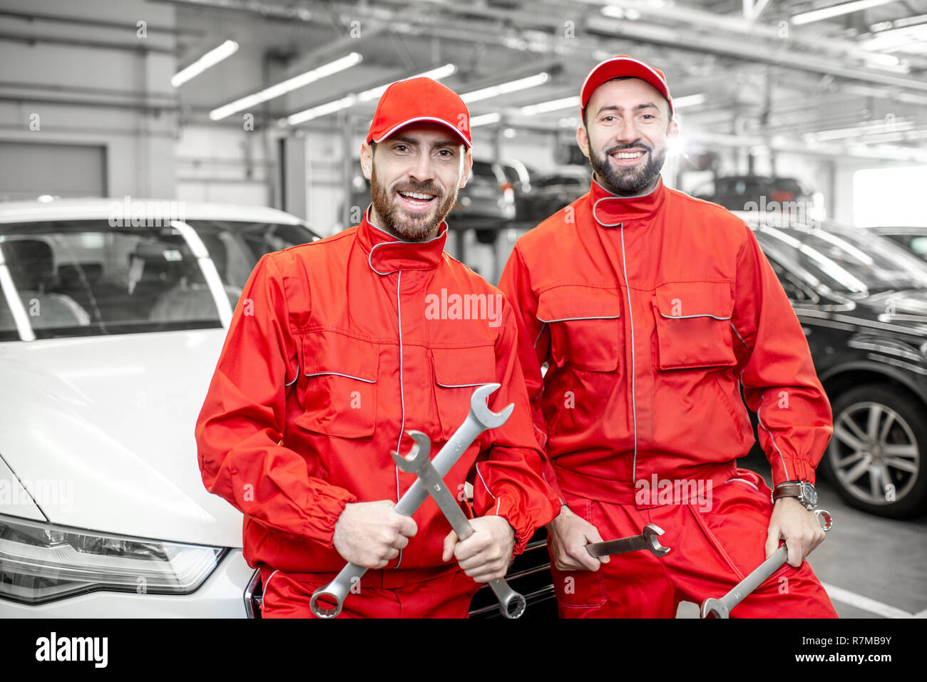 Portrait of a two handsome auto mechanics in red uniform standing with ...