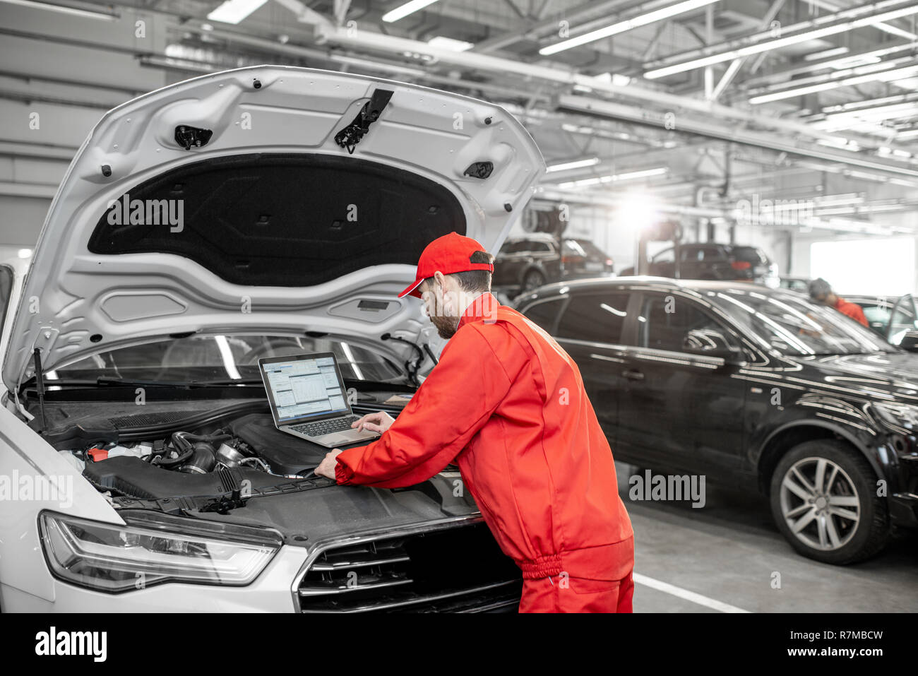 Handsome auto mechanic in red uniform doing engine diagnostics with ...