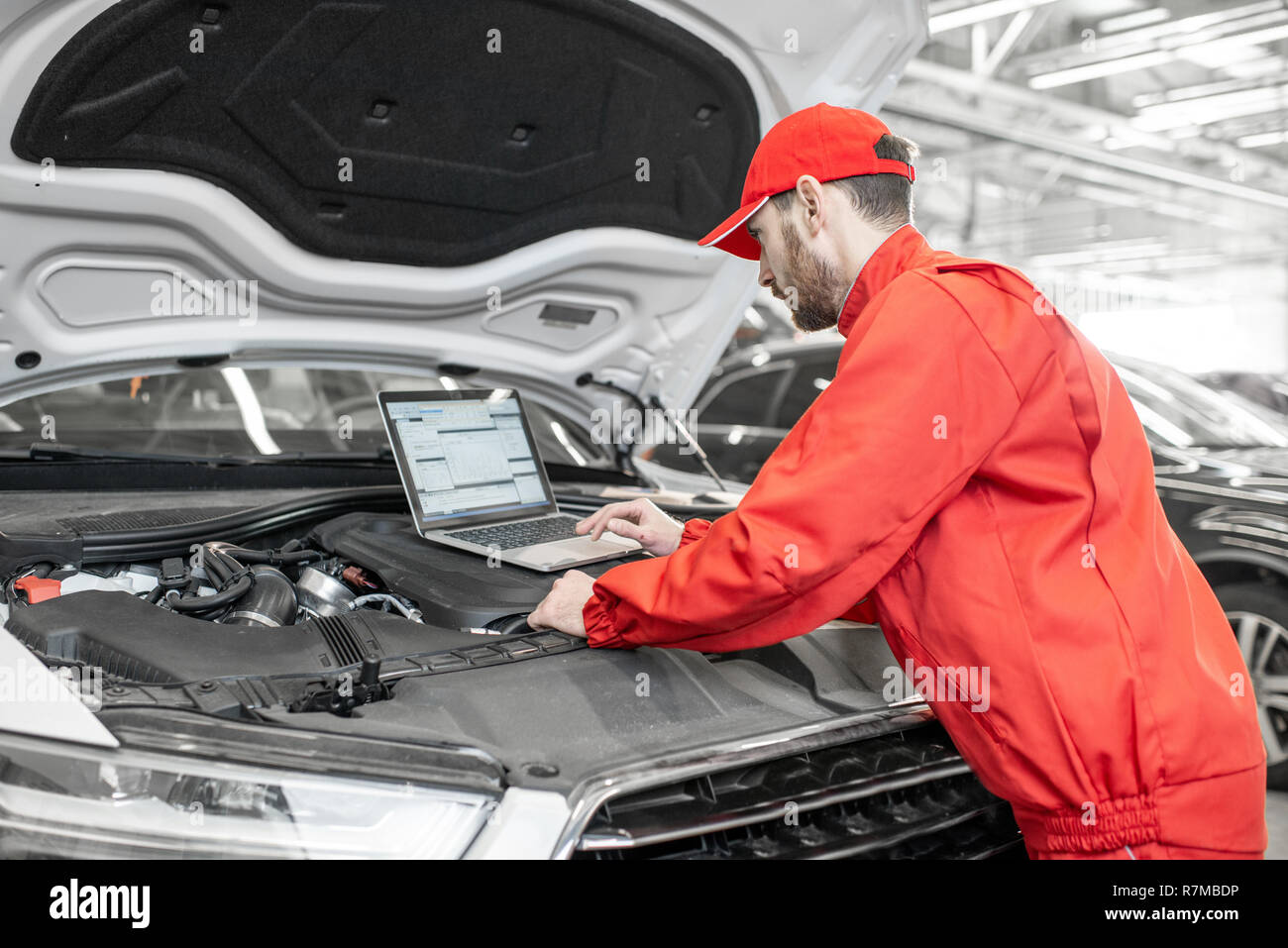 Handsome auto mechanic in red uniform doing engine diagnostics with ...