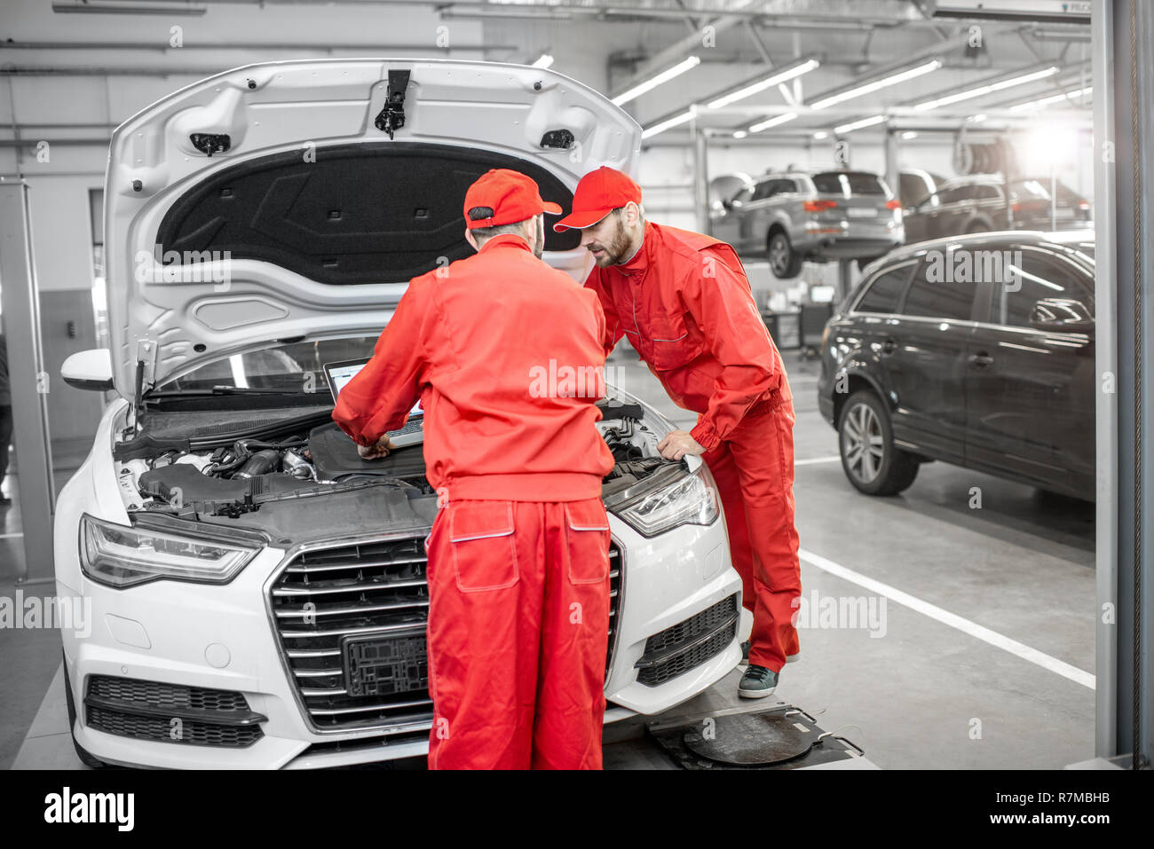 Two auto mechanics in red uniform doing engine diagnostics with ...