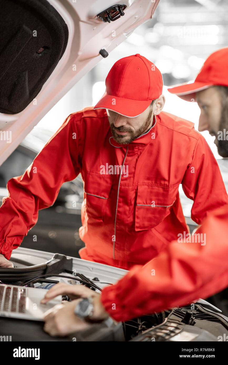 Two auto mechanics in red uniform doing engine diagnostics with ...