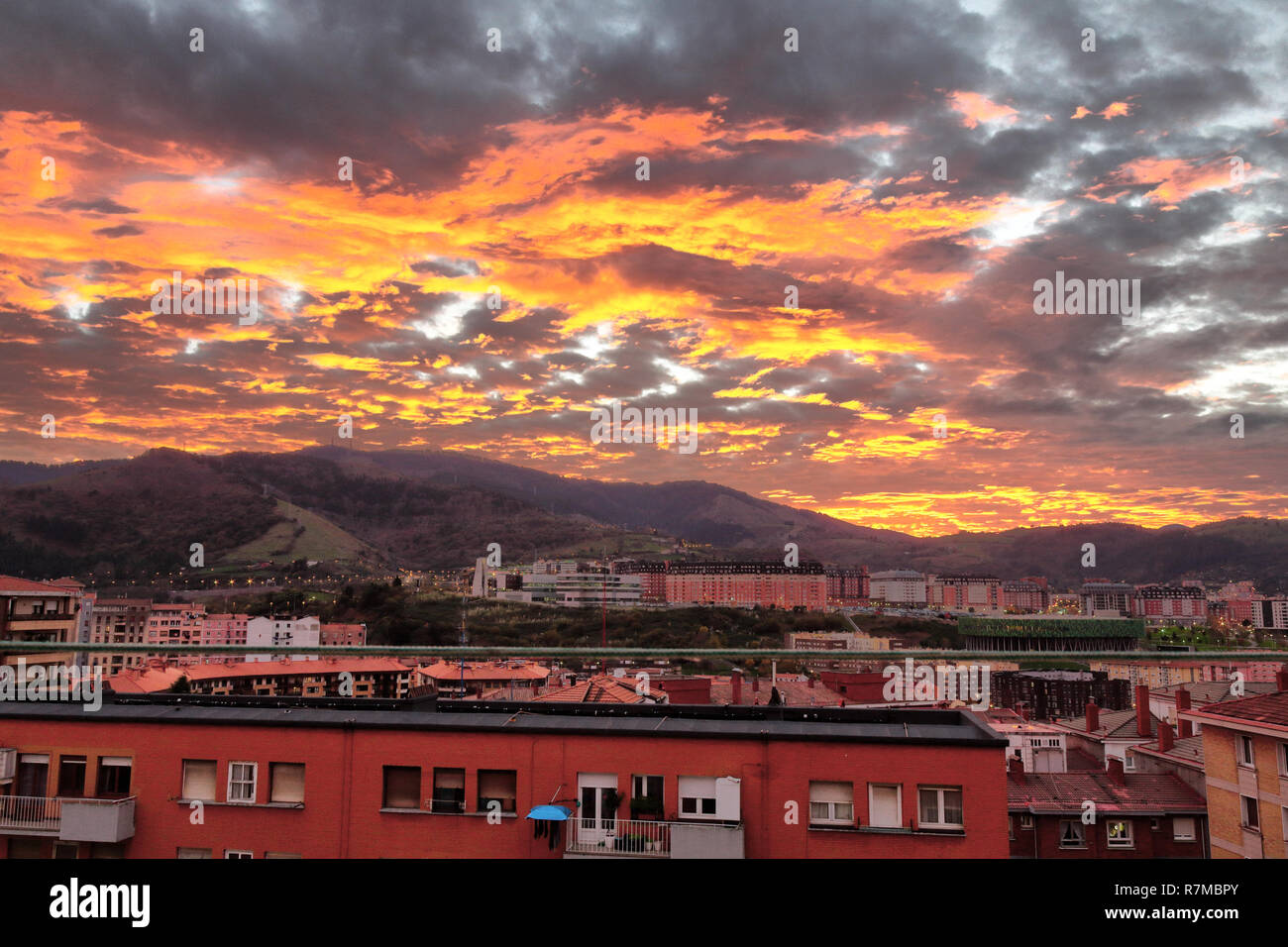 A landscape of Bilbao mountains and city centre with orange clouds ...