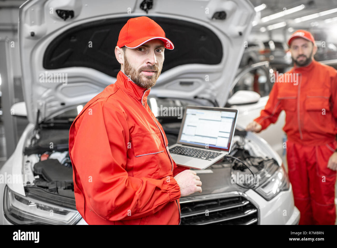 Two auto mechanics in red uniform doing engine diagnostics with ...