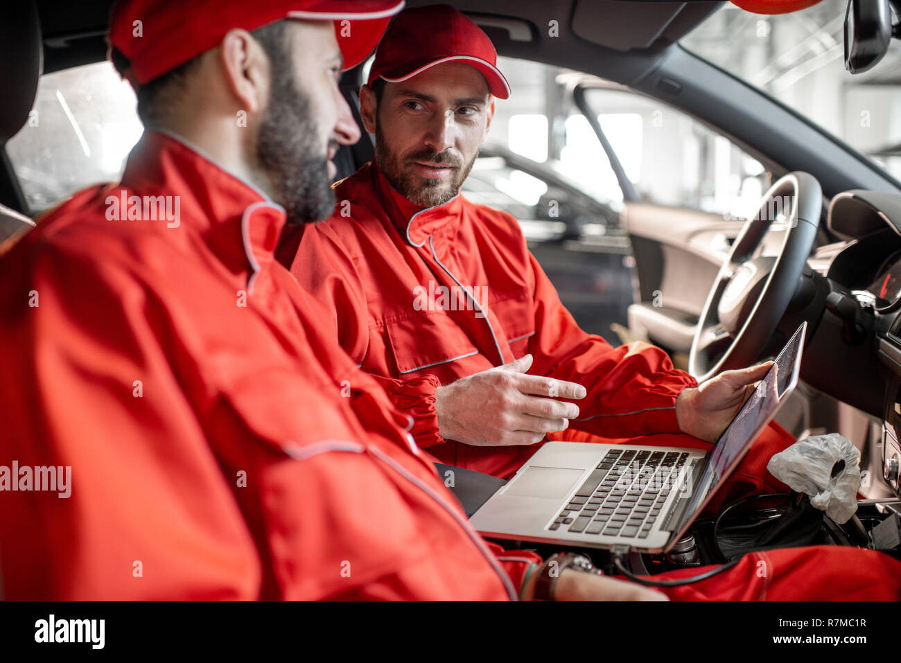 Two male auto mechanics in red uniform diagnosing car with computer ...